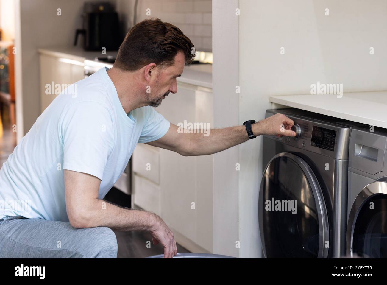 senior man adjusting washing machine settings at home, focusing on ...