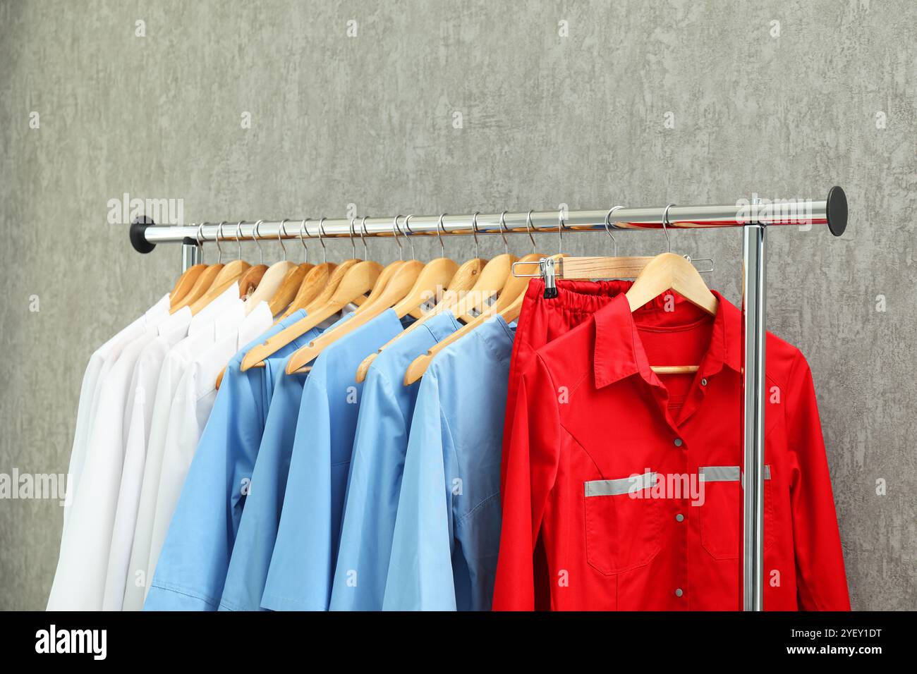 Different medical workers' uniforms on clothing rack against grey ...