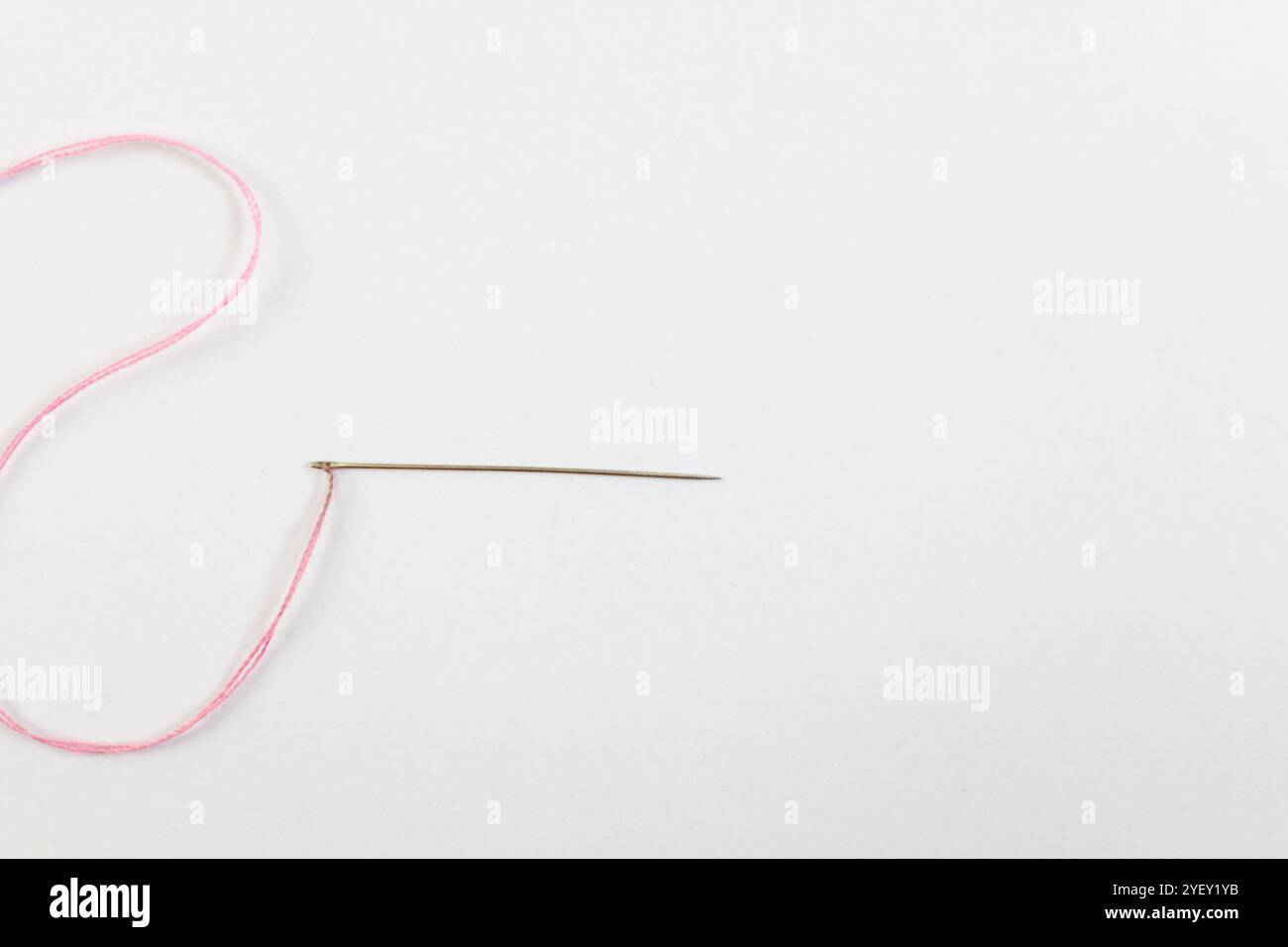 A single needle threaded with pink thread on a minimalist white ...
