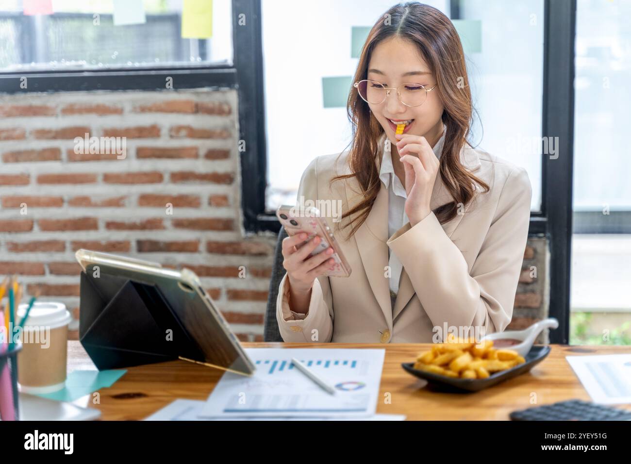 Young businesswoman eating unhealthy snack, french fried, while working ...