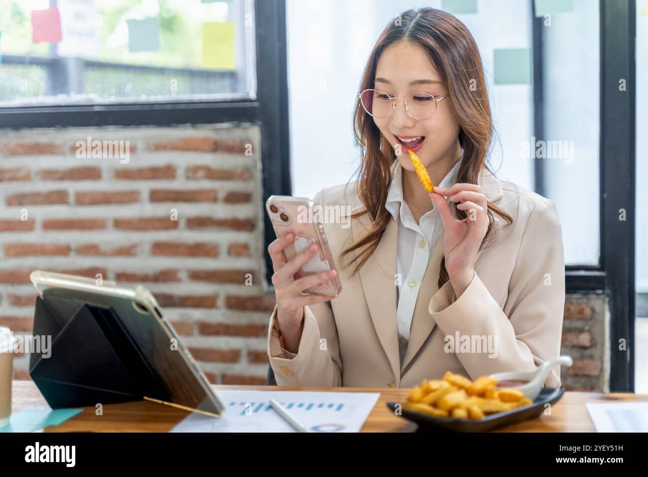 Young businesswoman eating unhealthy snack, french fried, while working ...