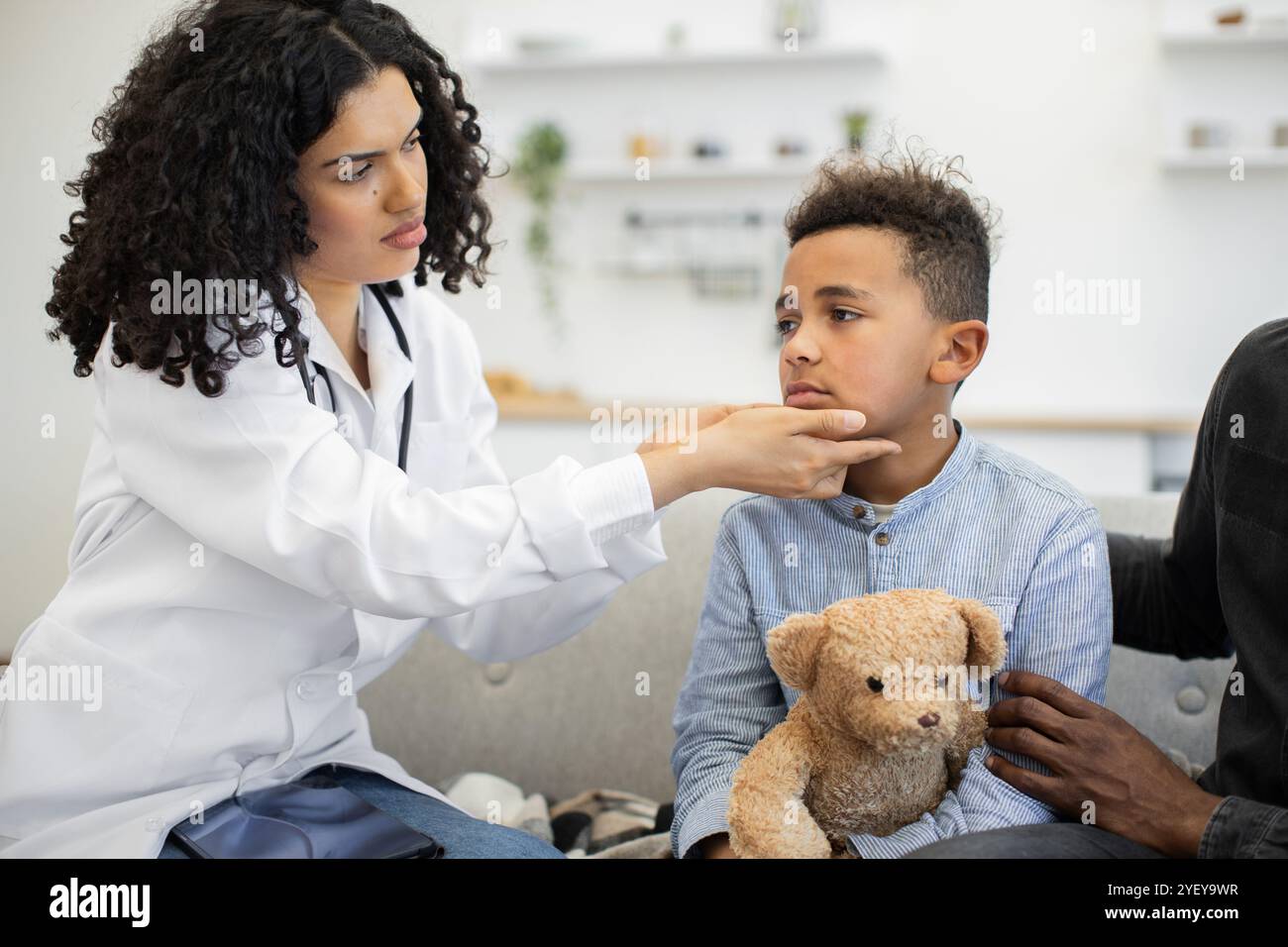 Female doctor examining boy's lymph nodes at home with concerned dad ...