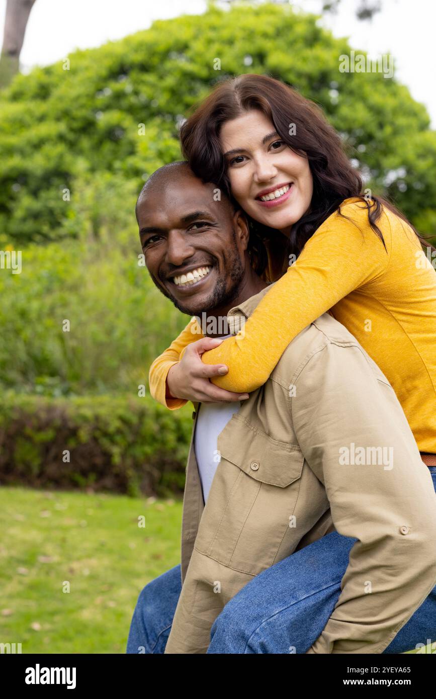 Smiling multiracial couple enjoying playful piggyback ride in lush ...