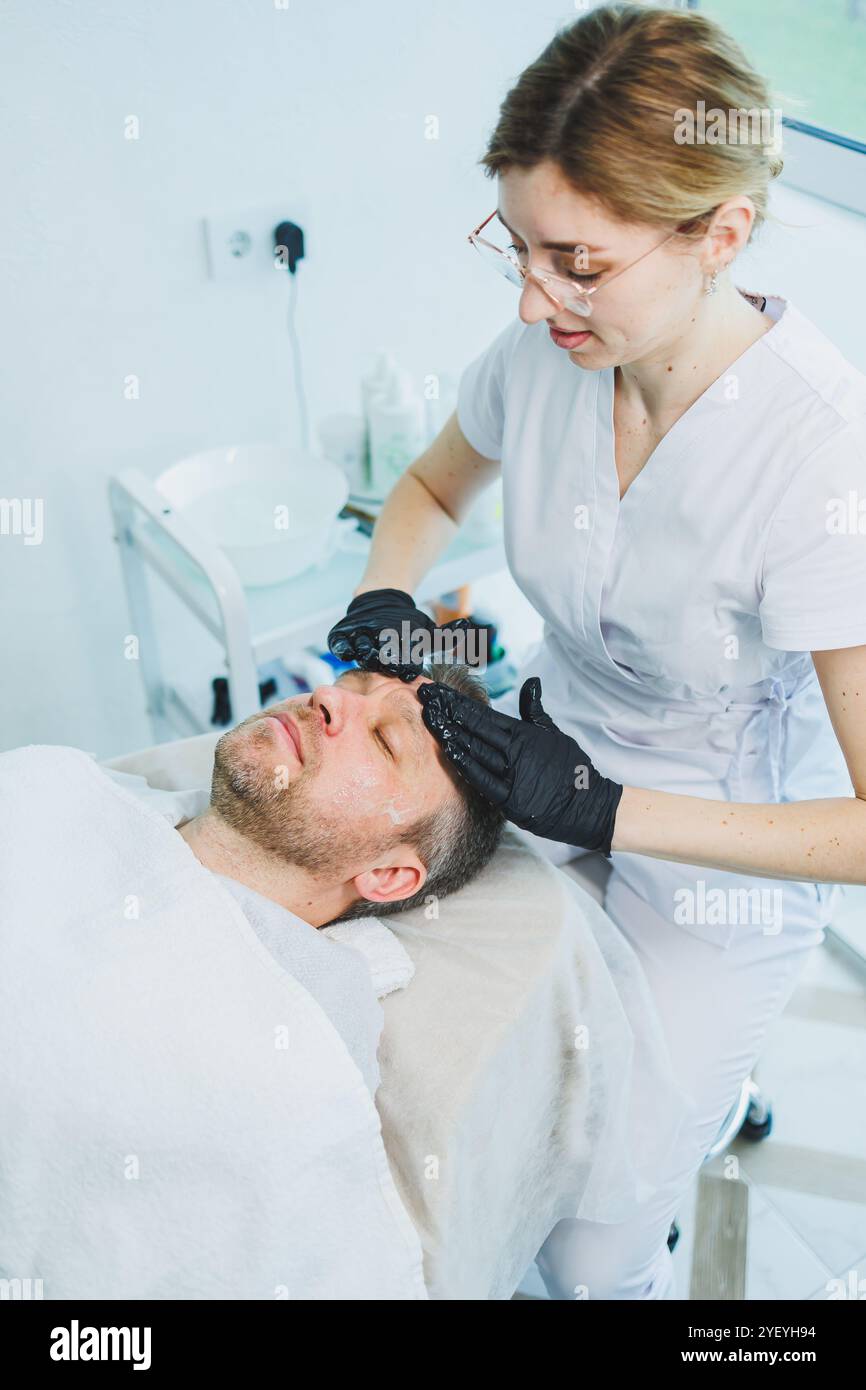 A beautician applies a medical mask to a man's face. Facial skin care ...