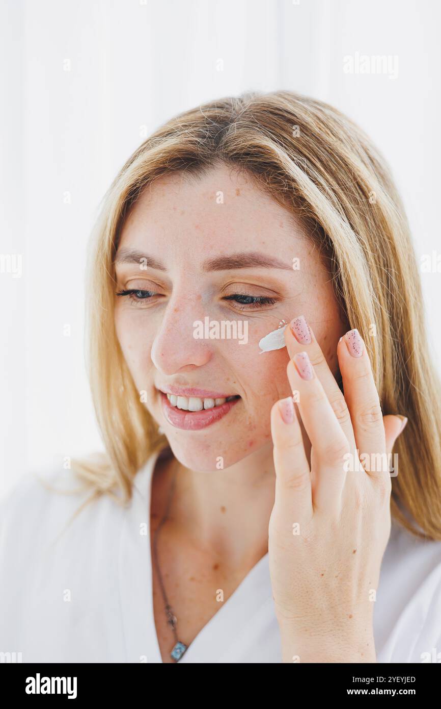 The face of a beautiful woman applying cosmetic cream to her skin ...
