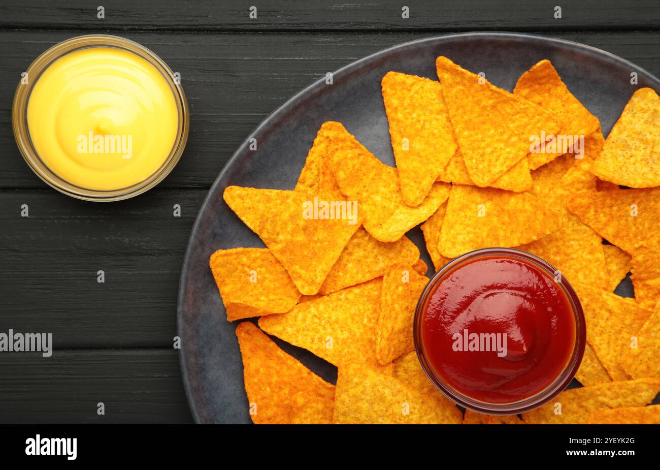 Nachos in plate with ketchup and cheese sause on black background ...