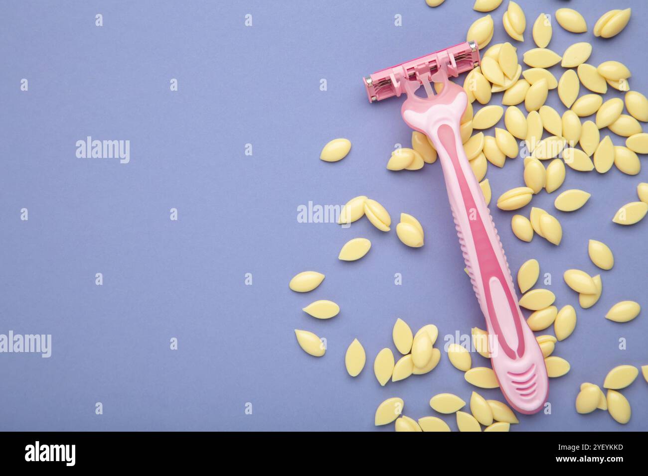 Wax granules for depilation with a razor on a purple background. Space ...