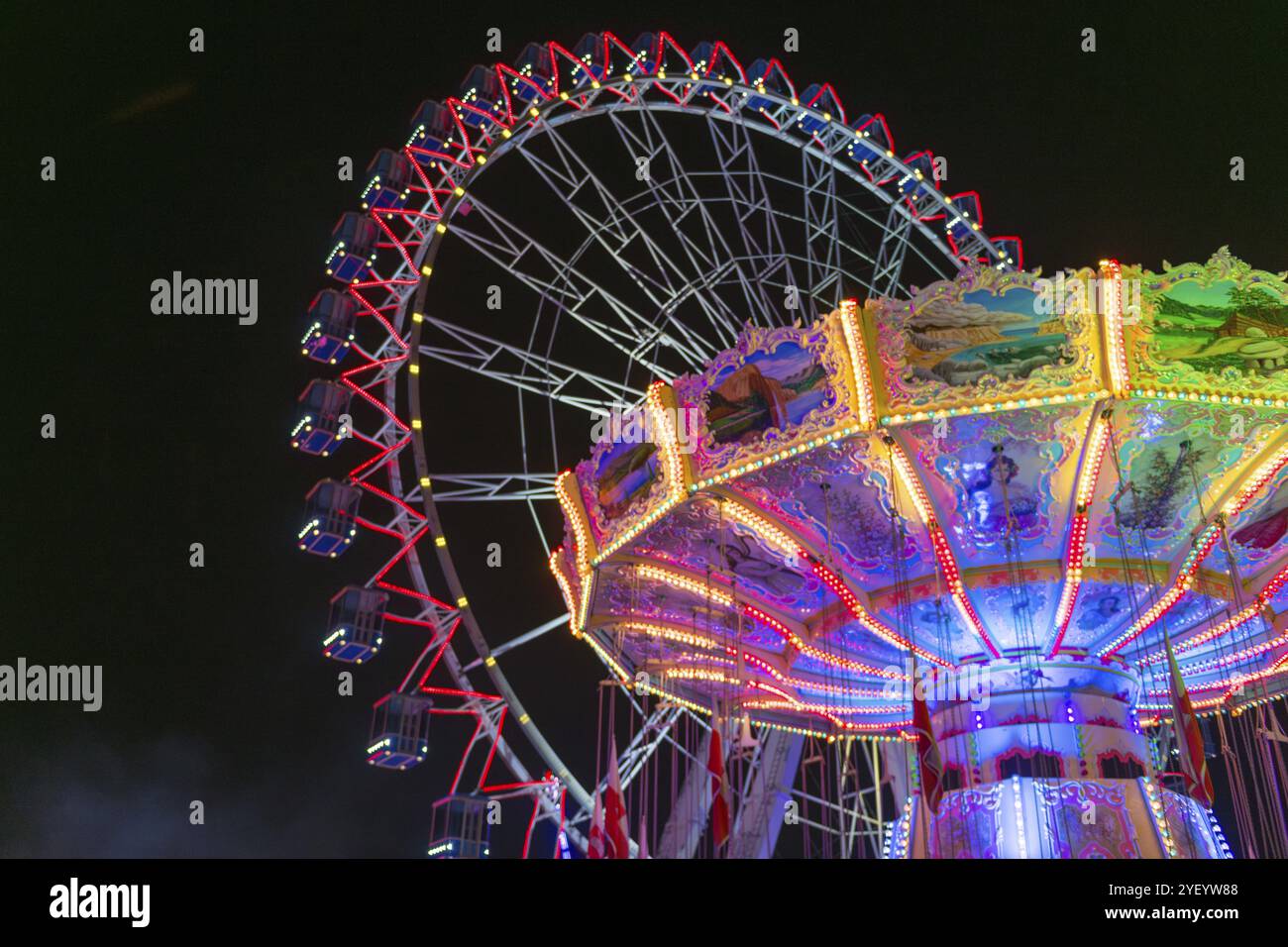 A funfair at night with illuminated chain carousel and Ferris wheel ...