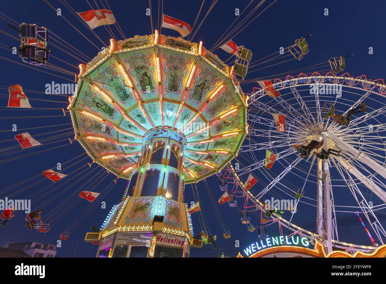 A funfair at dusk with illuminated chain carousel and Ferris wheel ...