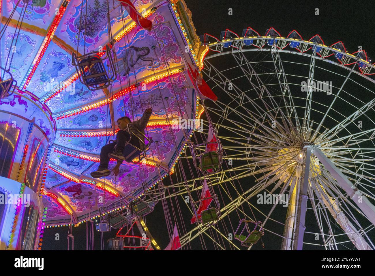 A funfair at dusk with illuminated chain carousel and Ferris wheel ...