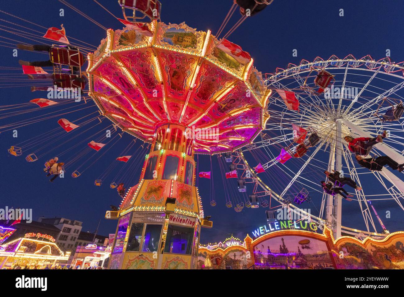 A funfair at dusk with illuminated chain carousel and Ferris wheel ...