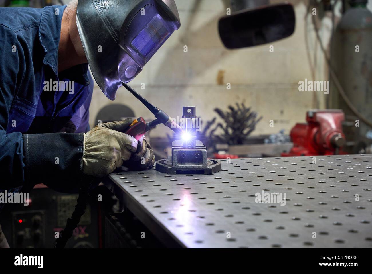 Metalworker wearing protective mask and gloves welding a custom ...