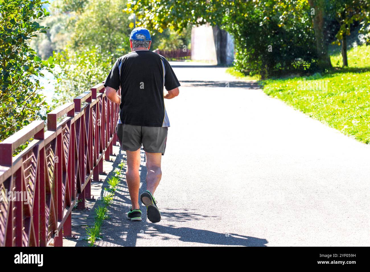 Elderly man jogging along a sunny park path, embracing a healthy and ...