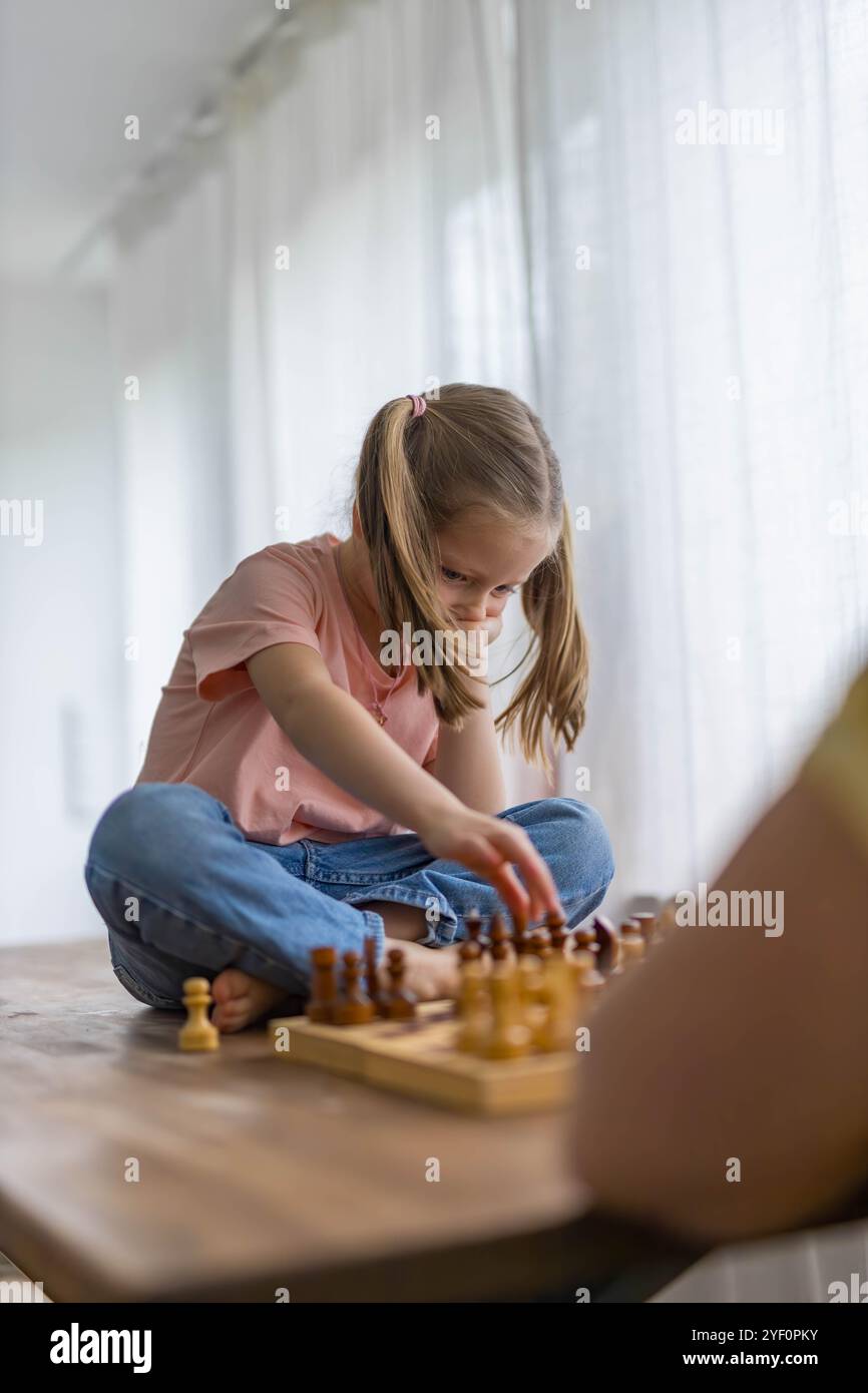 5-year-old girl plays with a mini chess set, focusing intently as she ...