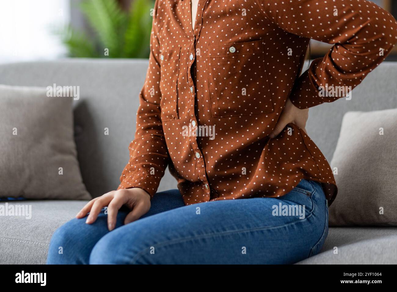 Woman experiencing back pain sitting on sofa, holding lower back ...
