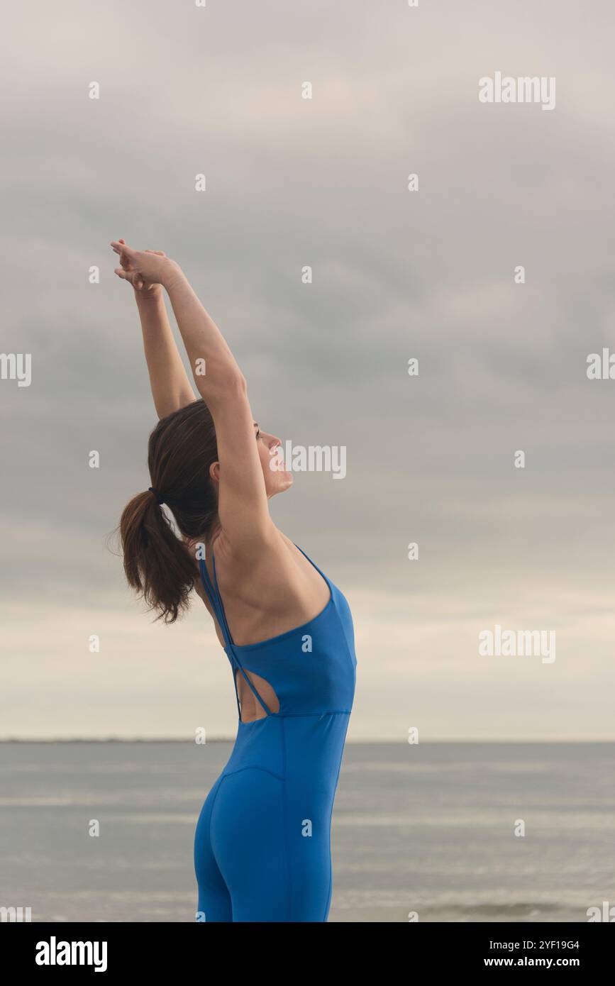 sporty woman swimmer doing an arm stretch above her head at the beach ...