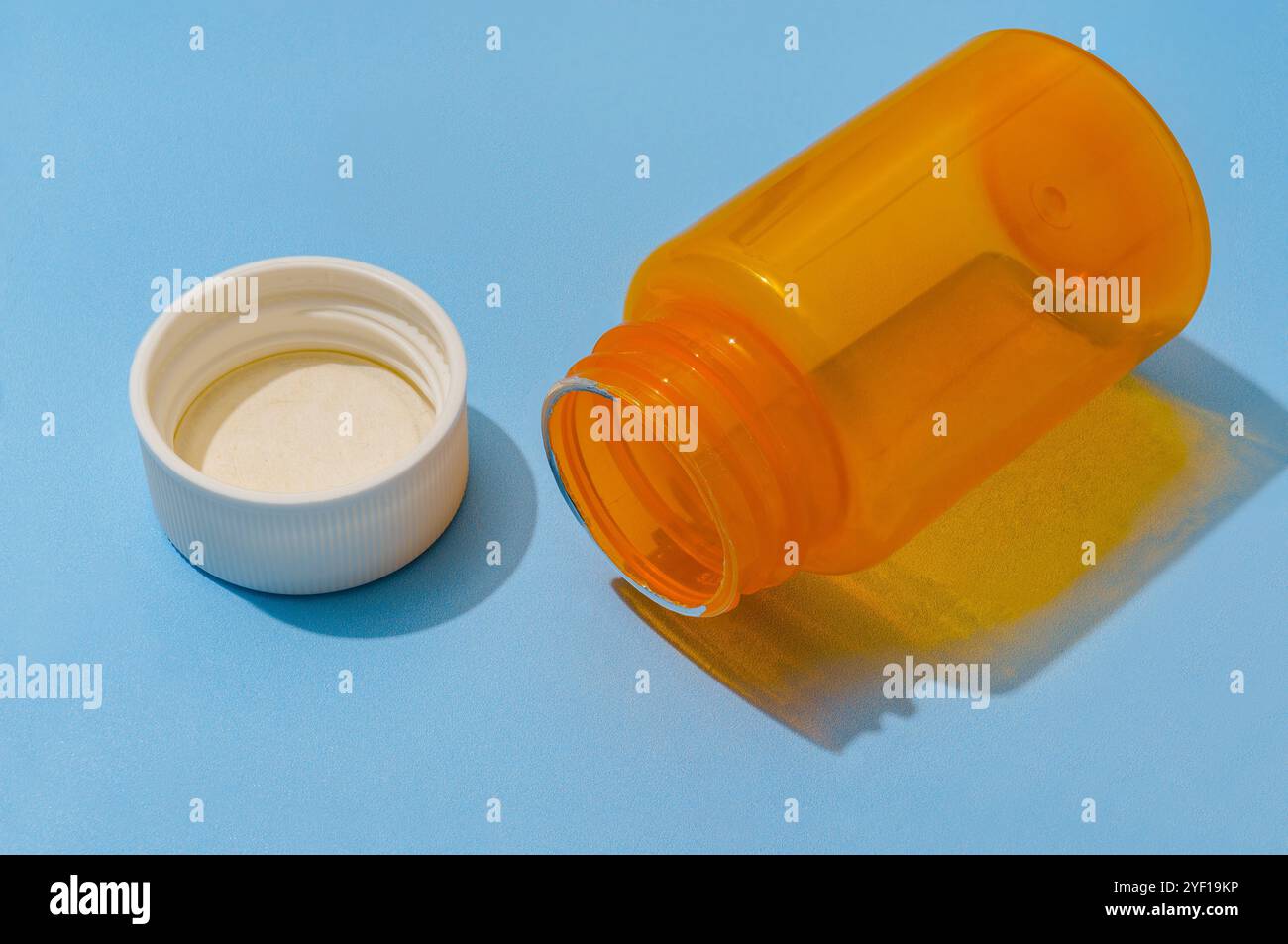 An empty orange plastic pill bottle lies on its side on a blue surface ...