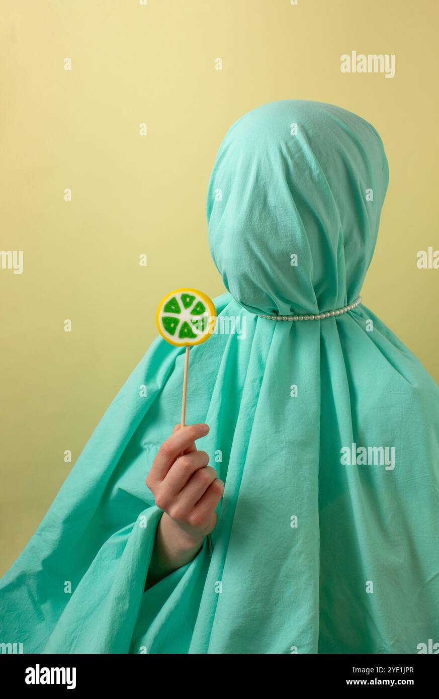 A human figure covered with a pastel mint sheet holds a lollipop in his ...