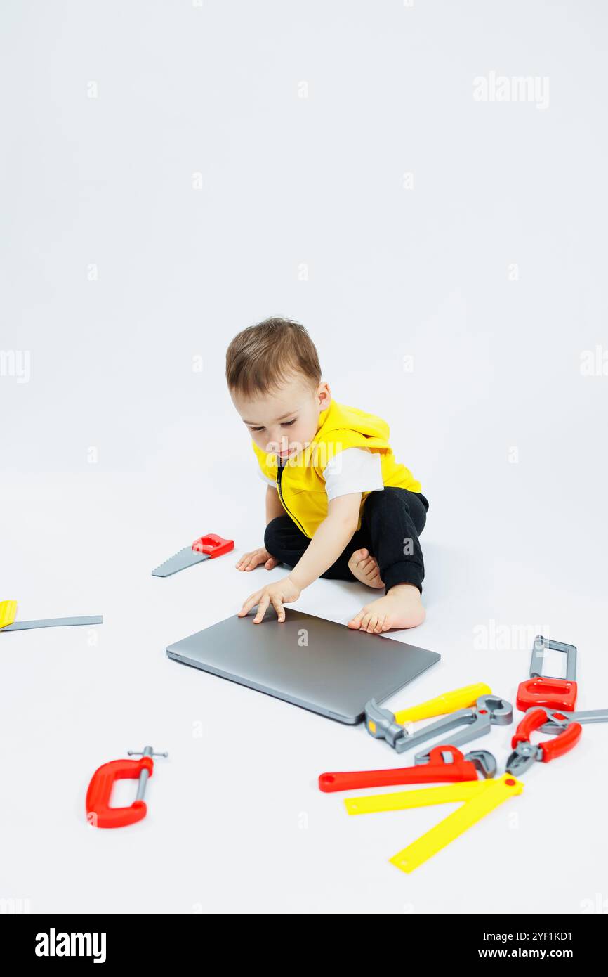 A cute 2-year-old boy is sitting at a digital laptop on a white ...