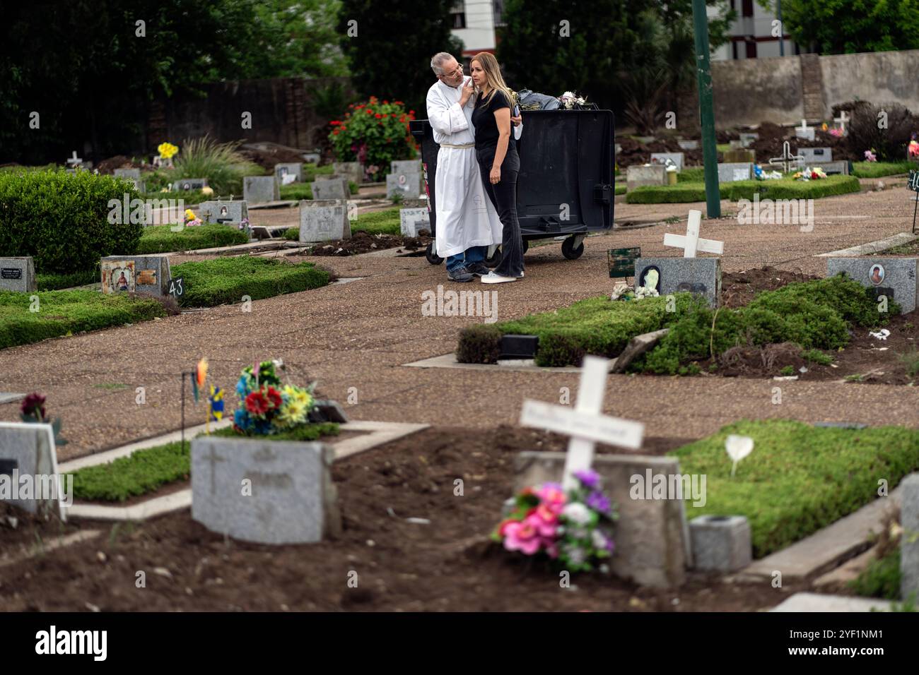A priest comforts a woman who arrived at the cemetery to visit the ...