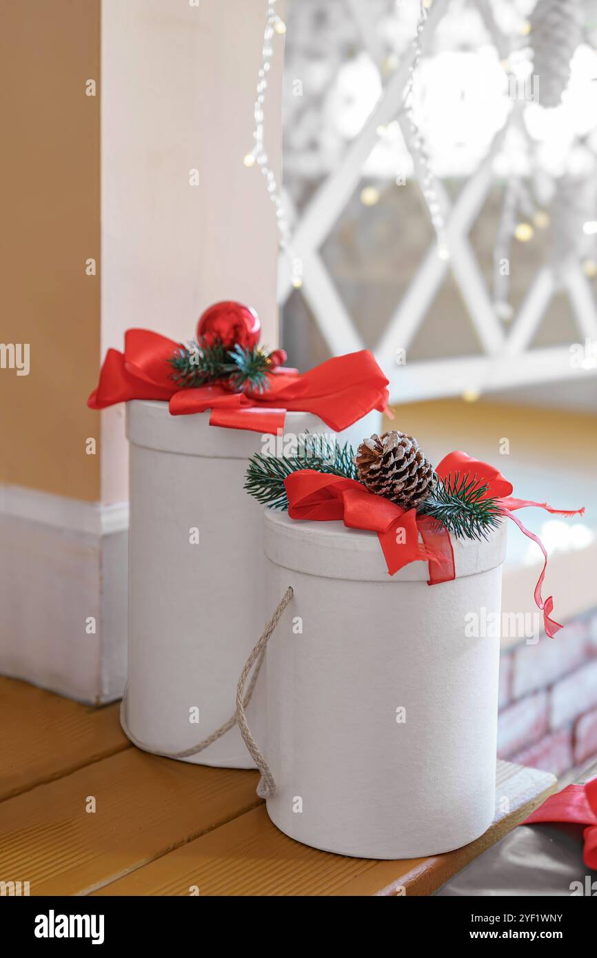 Two round white gift boxes decorated with red bows, spruce branch and ...