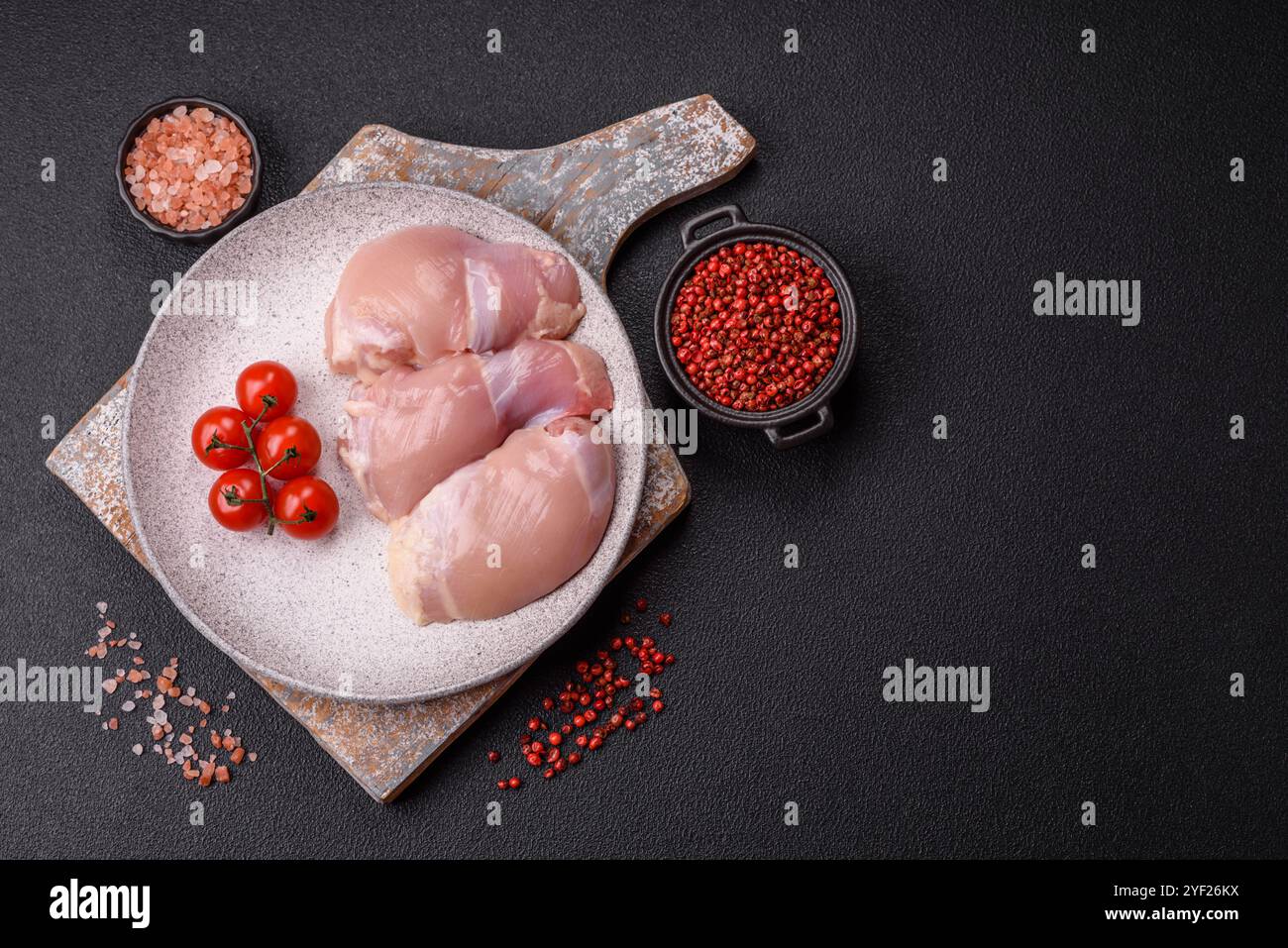 Fresh raw chicken thigh fillets with salt, spices and herbs on a dark ...