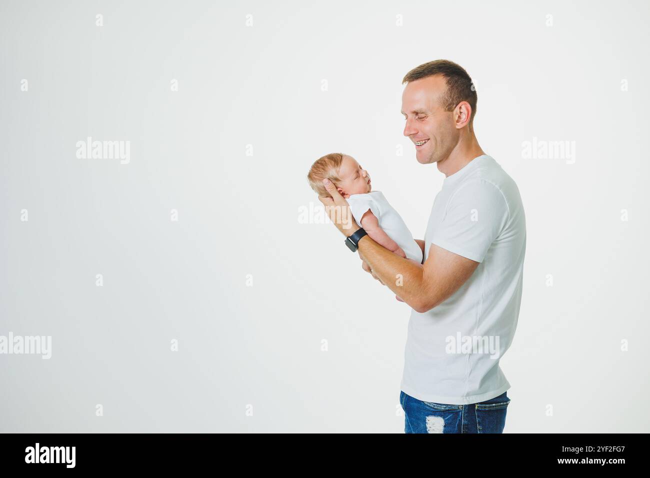 A young dad holds a newborn baby in his hands on a white background ...