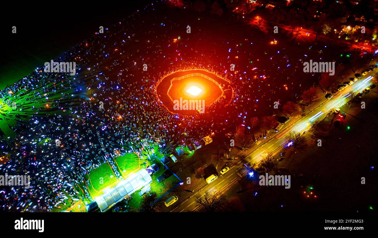 An aerial nighttime view of a large crowd gathered around a bonfire in ...