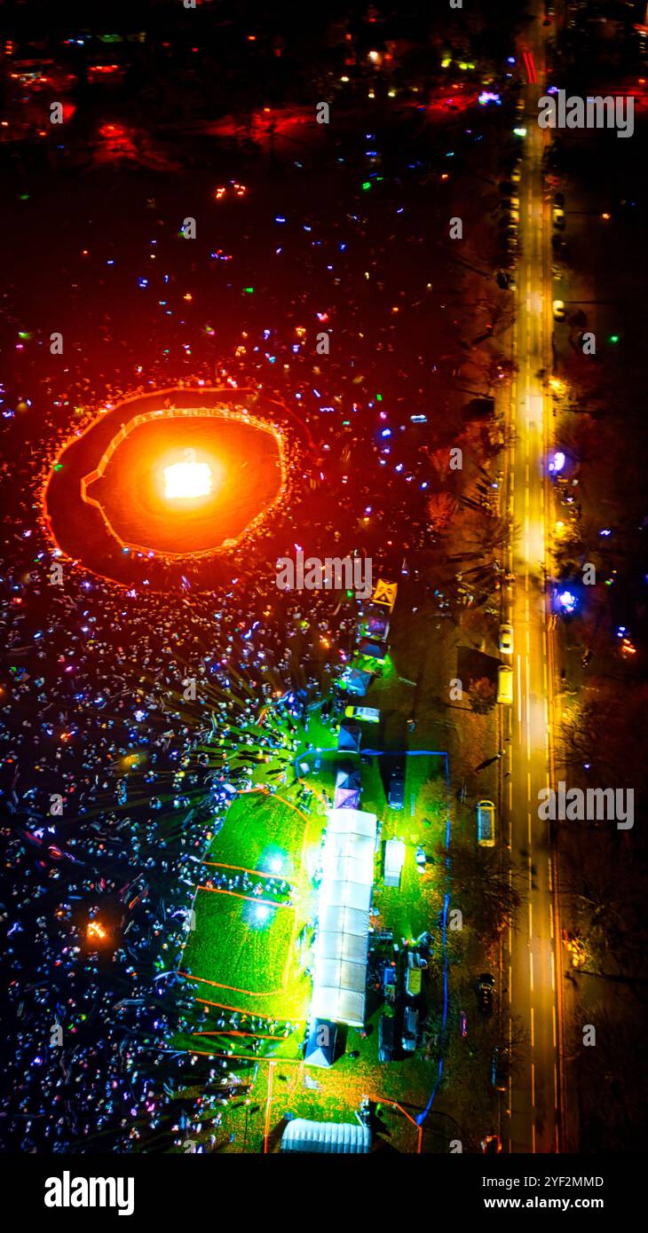 Aerial night view of a large crowd gathered around a bonfire, with a ...