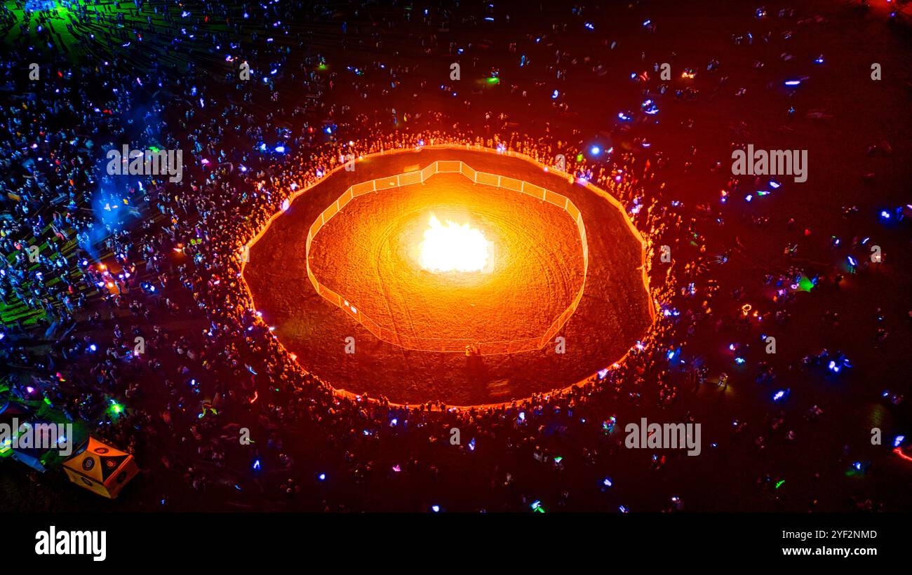 Aerial view of a large bonfire in a field at night. People surround the ...