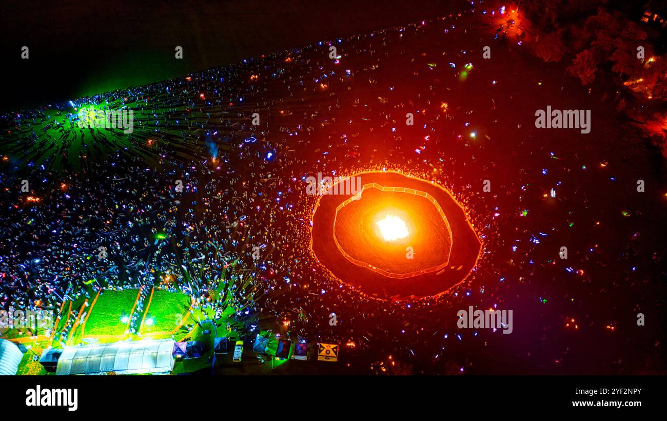 Aerial nighttime view of a large crowd gathered around a bonfire with ...