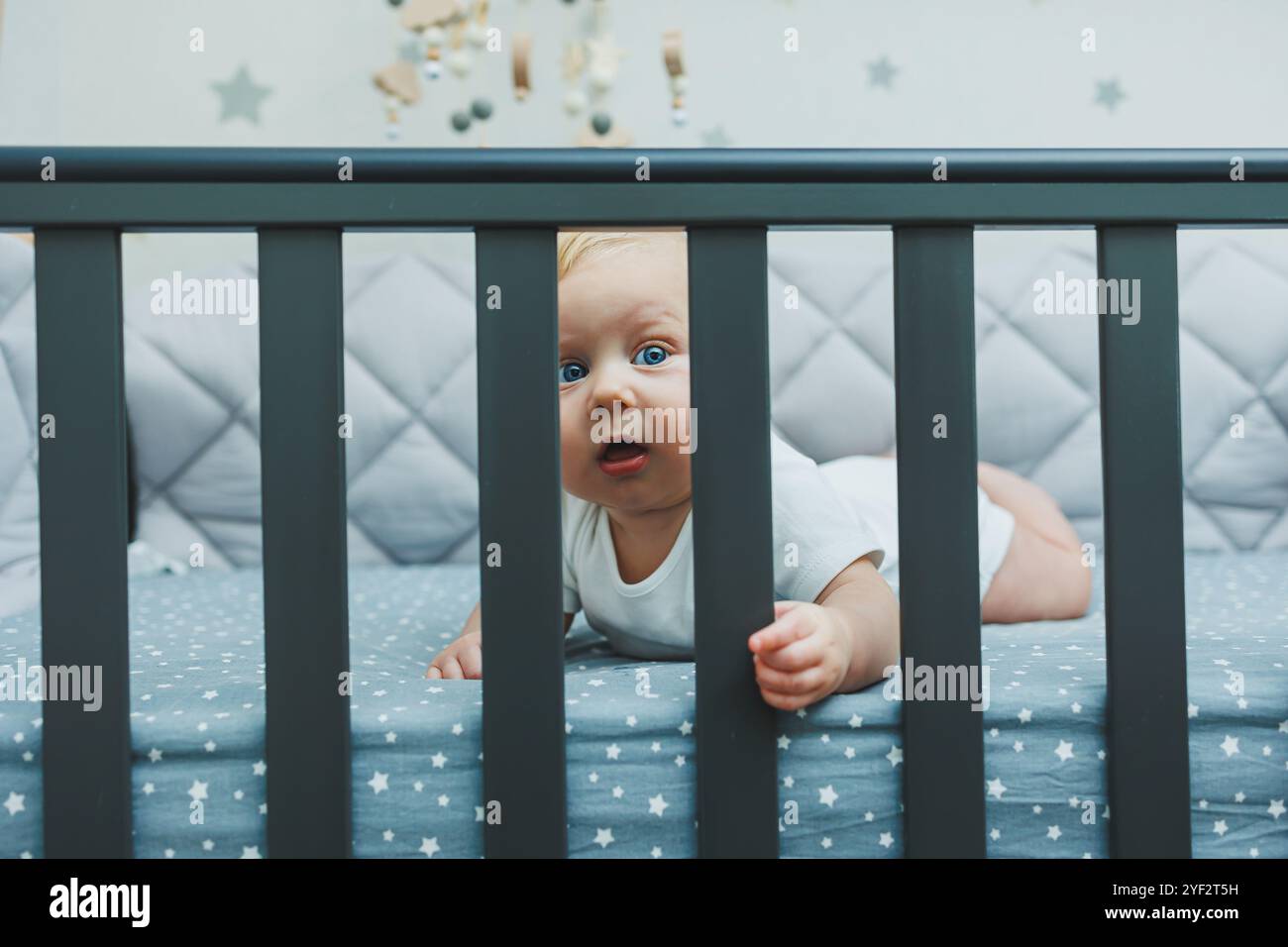 The baby looks through the sides of the crib into the room. A small ...