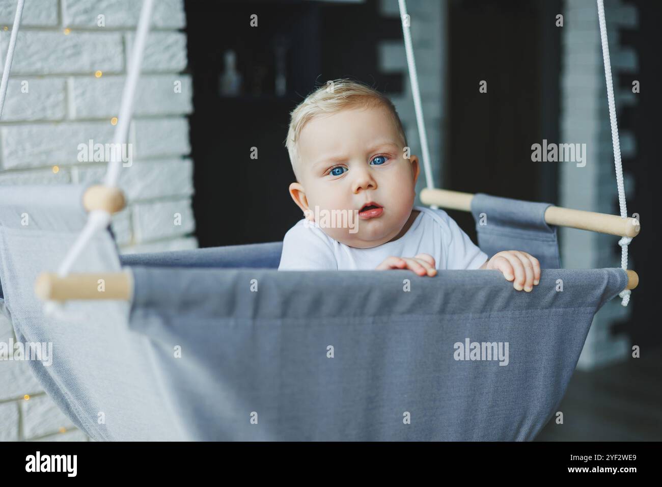 Baby boy swings in a swing at home. The child learns to have fun. Child ...