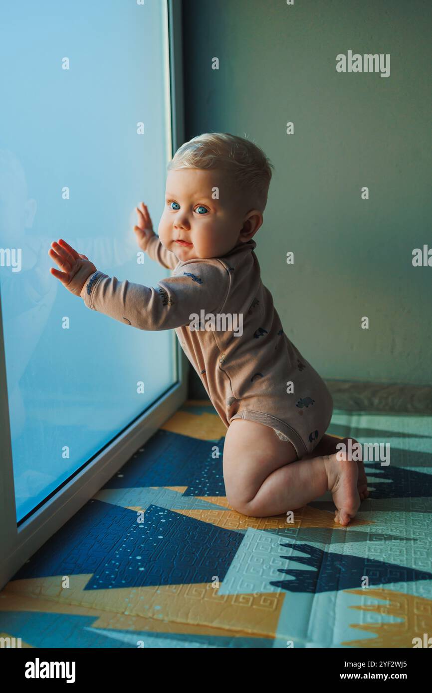 A baby boy tries to stand up by the window. The child learns to stand ...