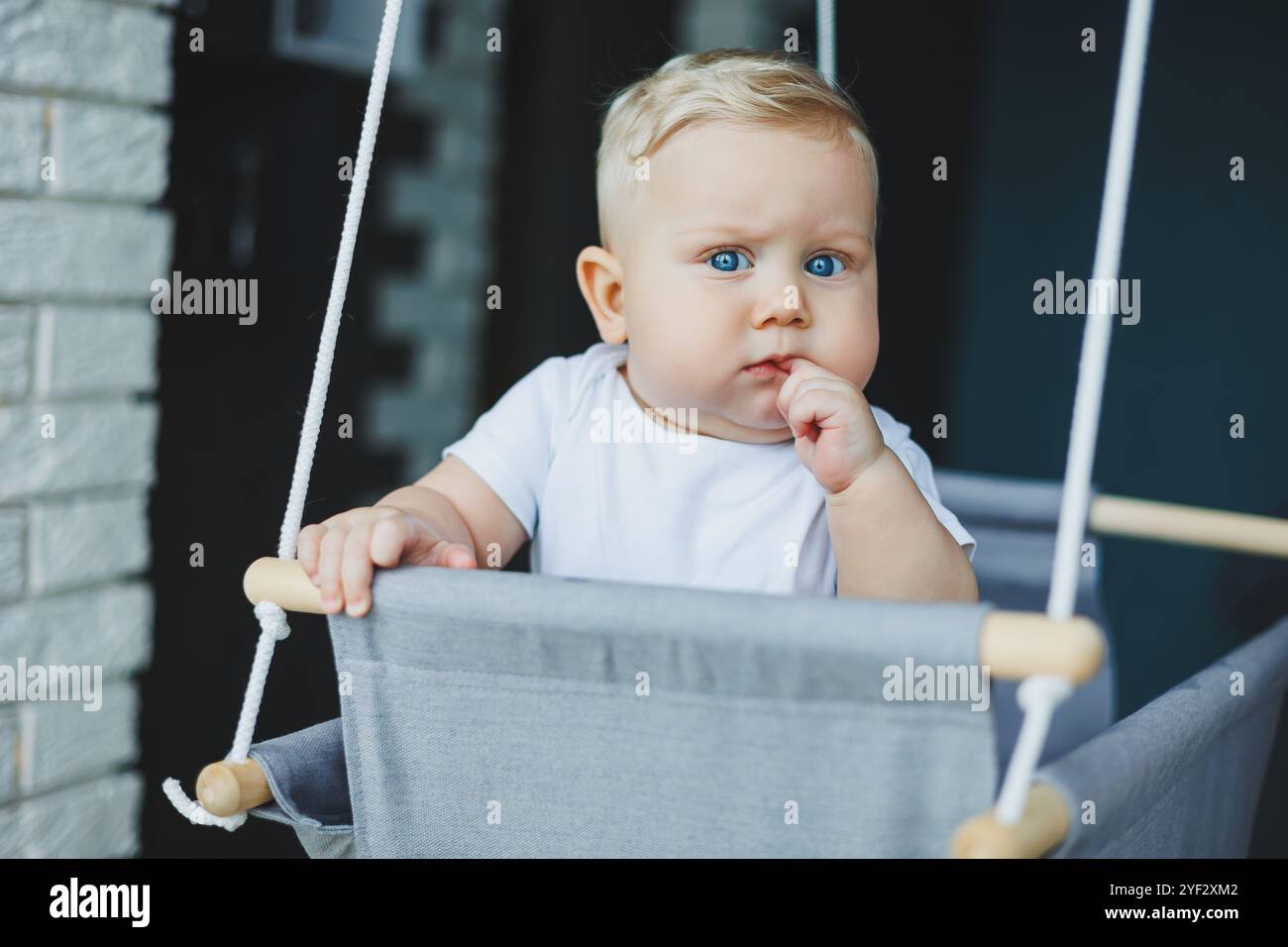 Baby boy swings on a swing at home. A child rides on a swing at home ...