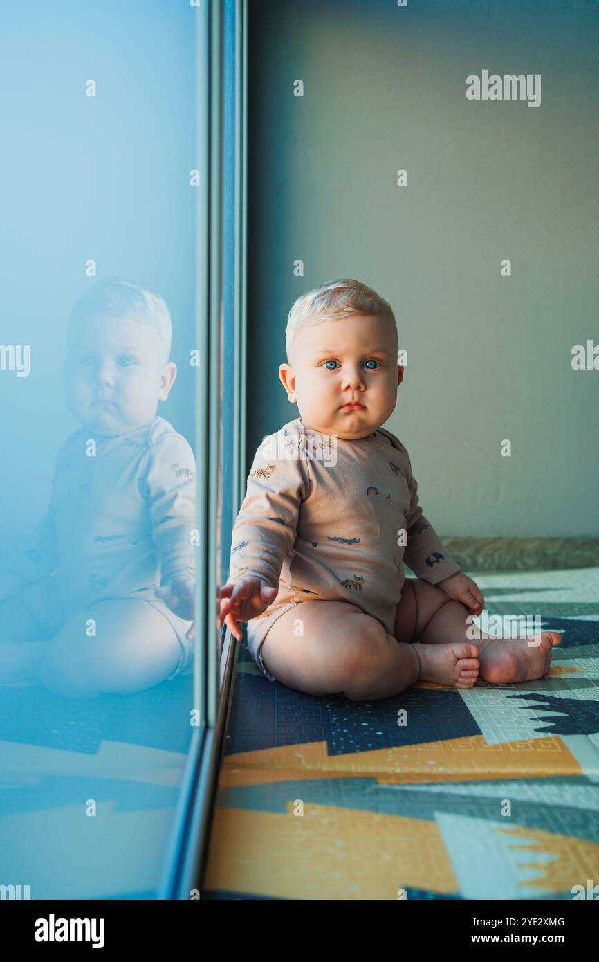 A baby boy tries to stand up by the window. The child learns to stand ...
