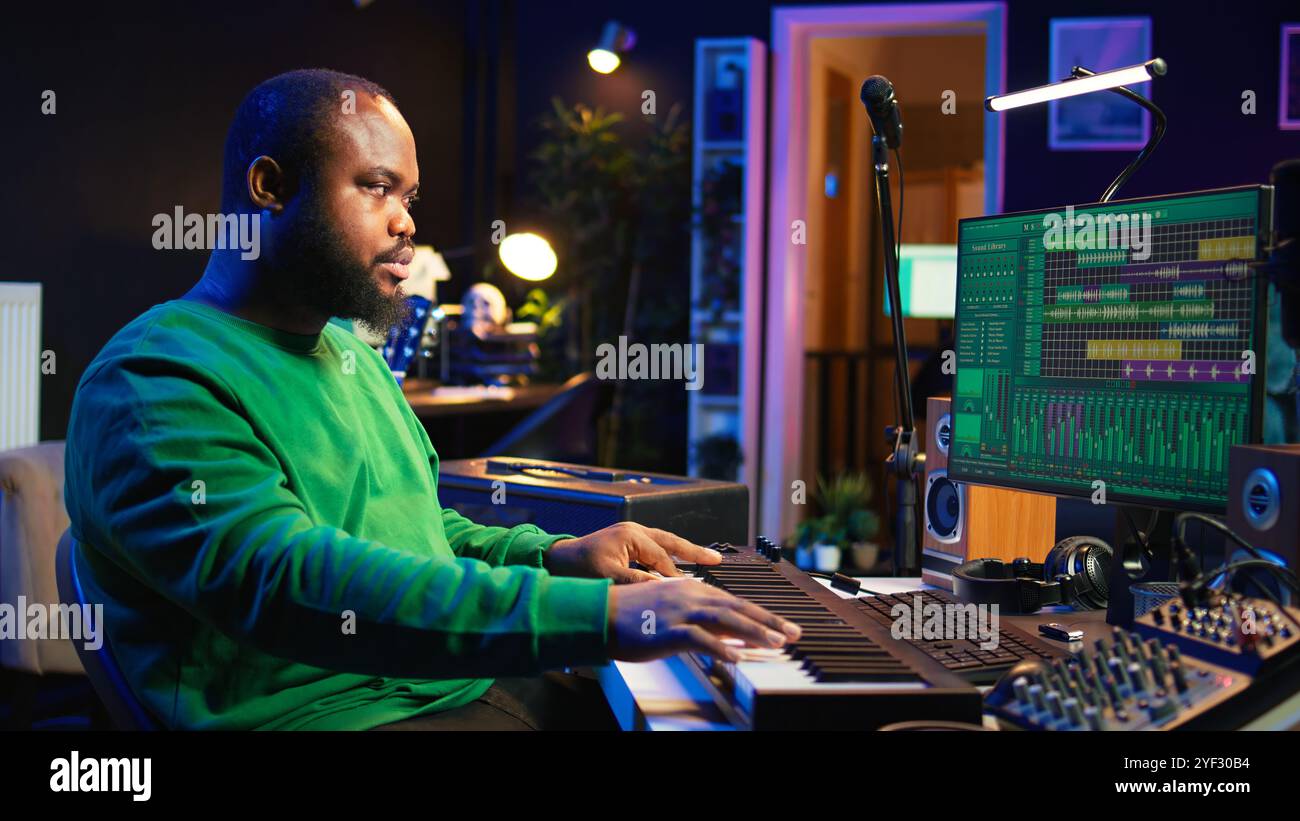 Male artist producing music on electronic piano keyboard in home studio ...