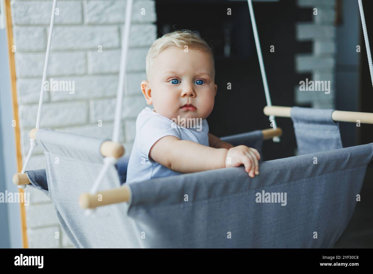 Baby boy swings on a swing at home. A child rides on a swing at home ...