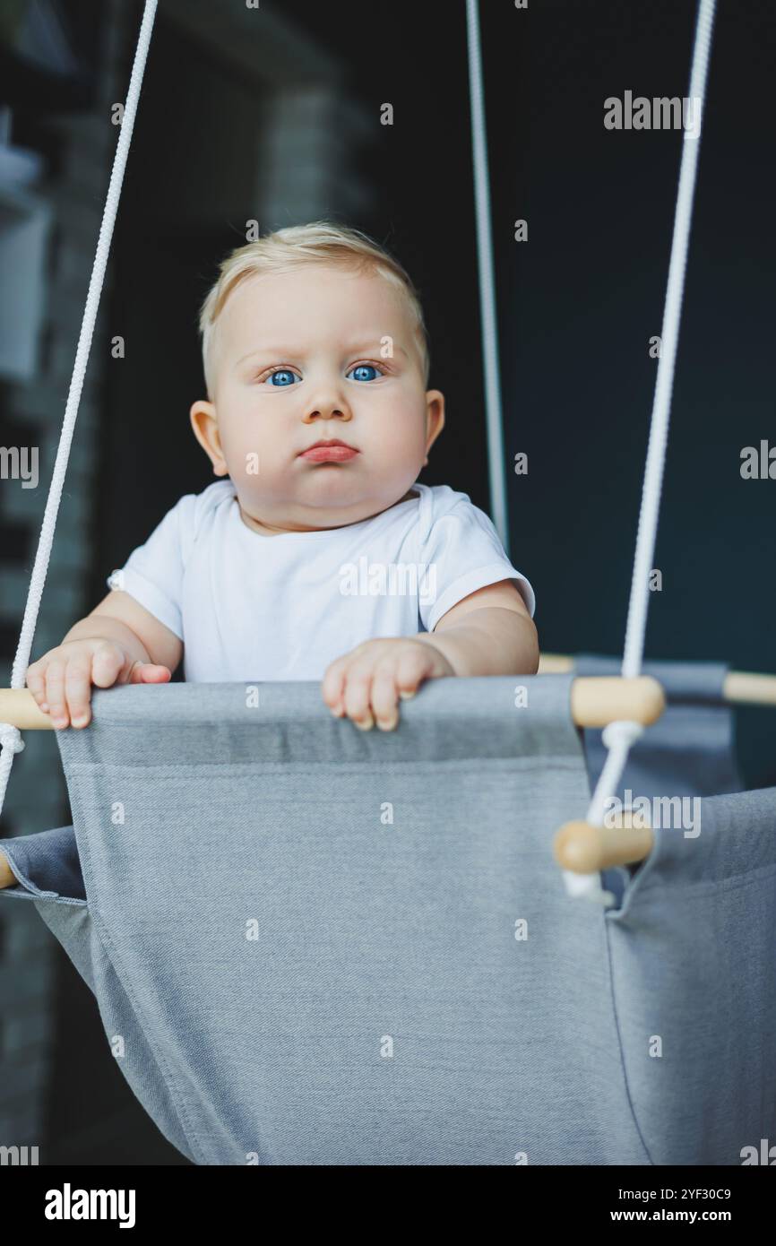 Baby boy swings on a swing at home. A child rides on a swing at home ...