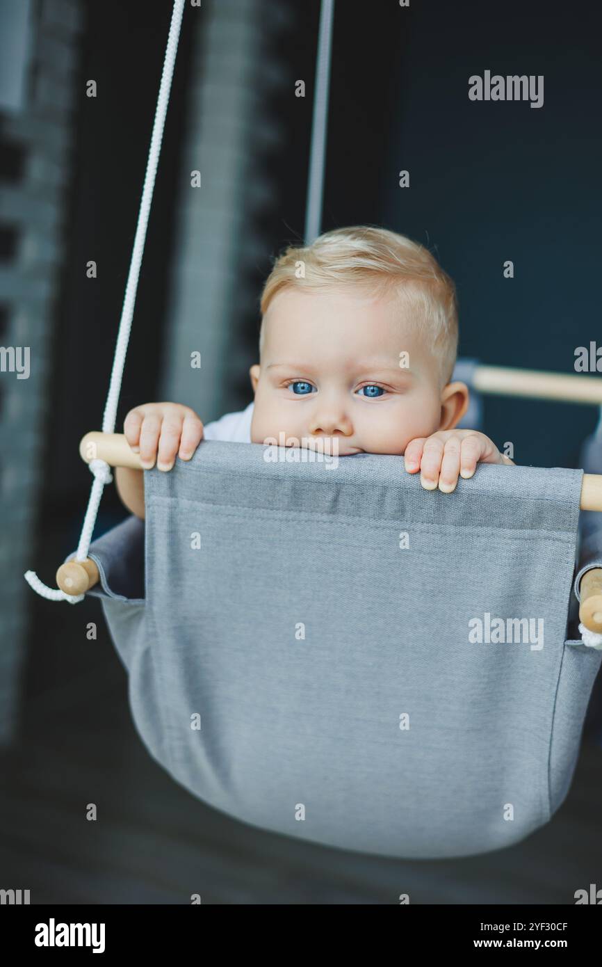 Baby boy swings on a swing at home. A child rides on a swing at home ...