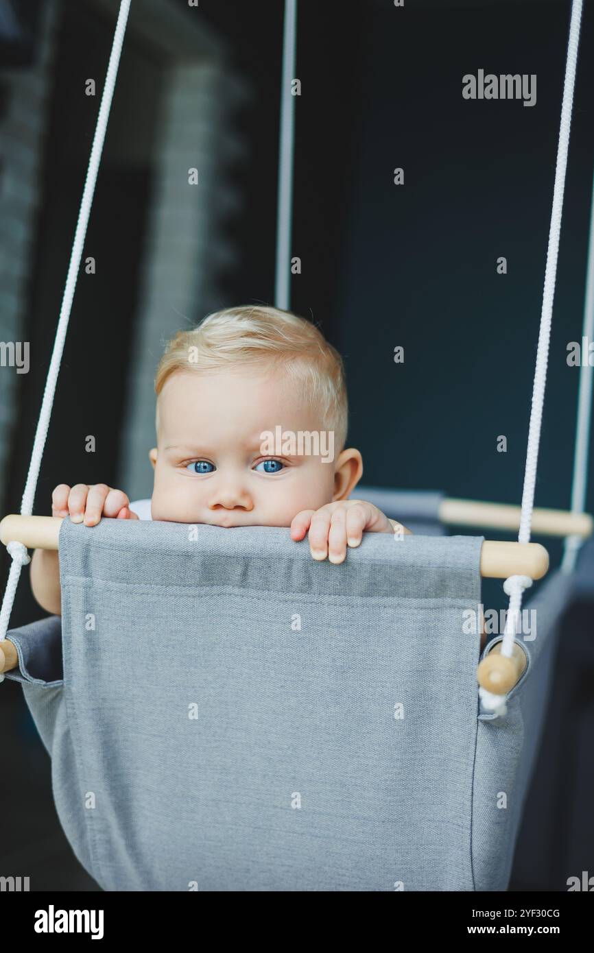 Baby boy swings on a swing at home. A child rides on a swing at home ...