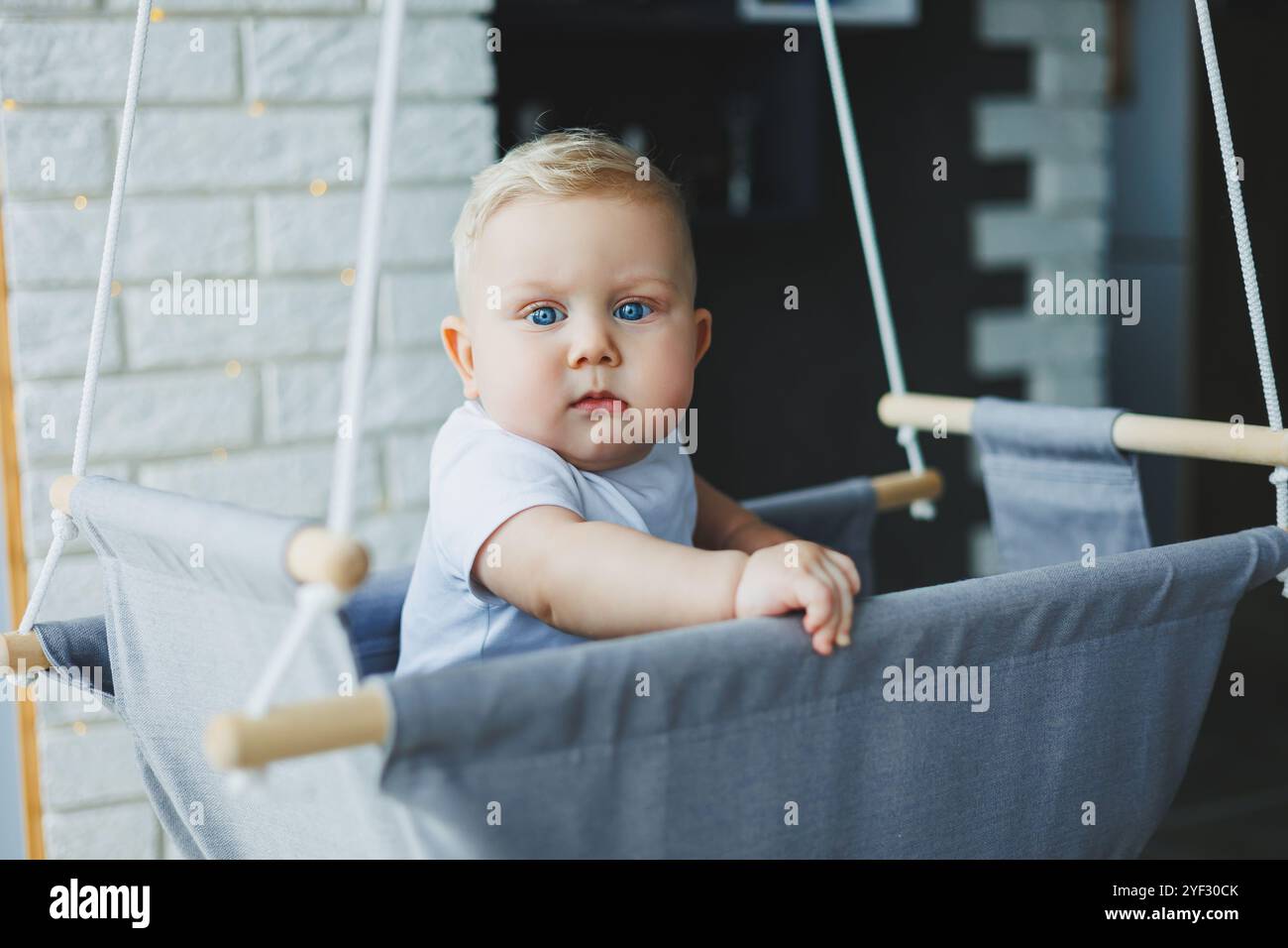 Baby boy swings on a swing at home. A child rides on a swing at home ...
