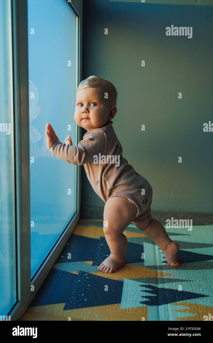A baby boy tries to stand up by the window. The child learns to stand ...