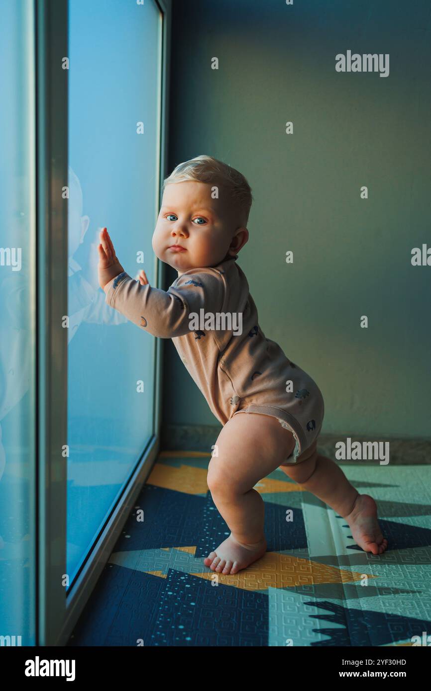 A baby boy tries to stand up by the window. The child learns to stand ...