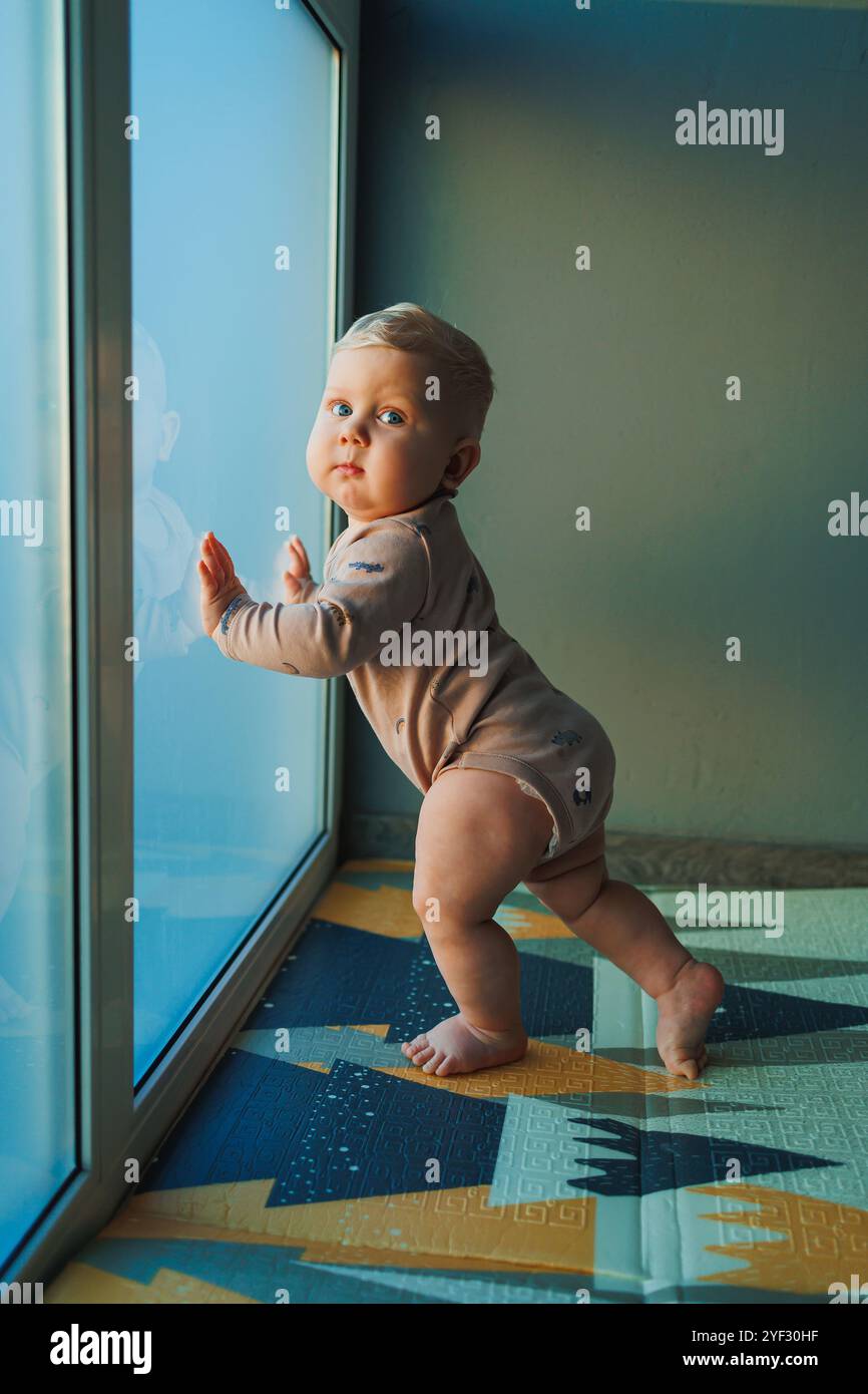 A baby boy tries to stand up by the window. The child learns to stand ...