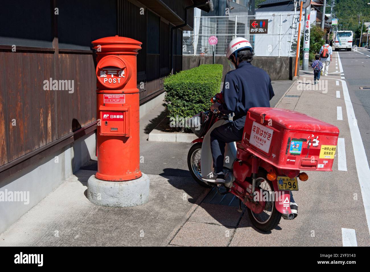 Japanese postman on a red motor scooter picking up mail at a ...