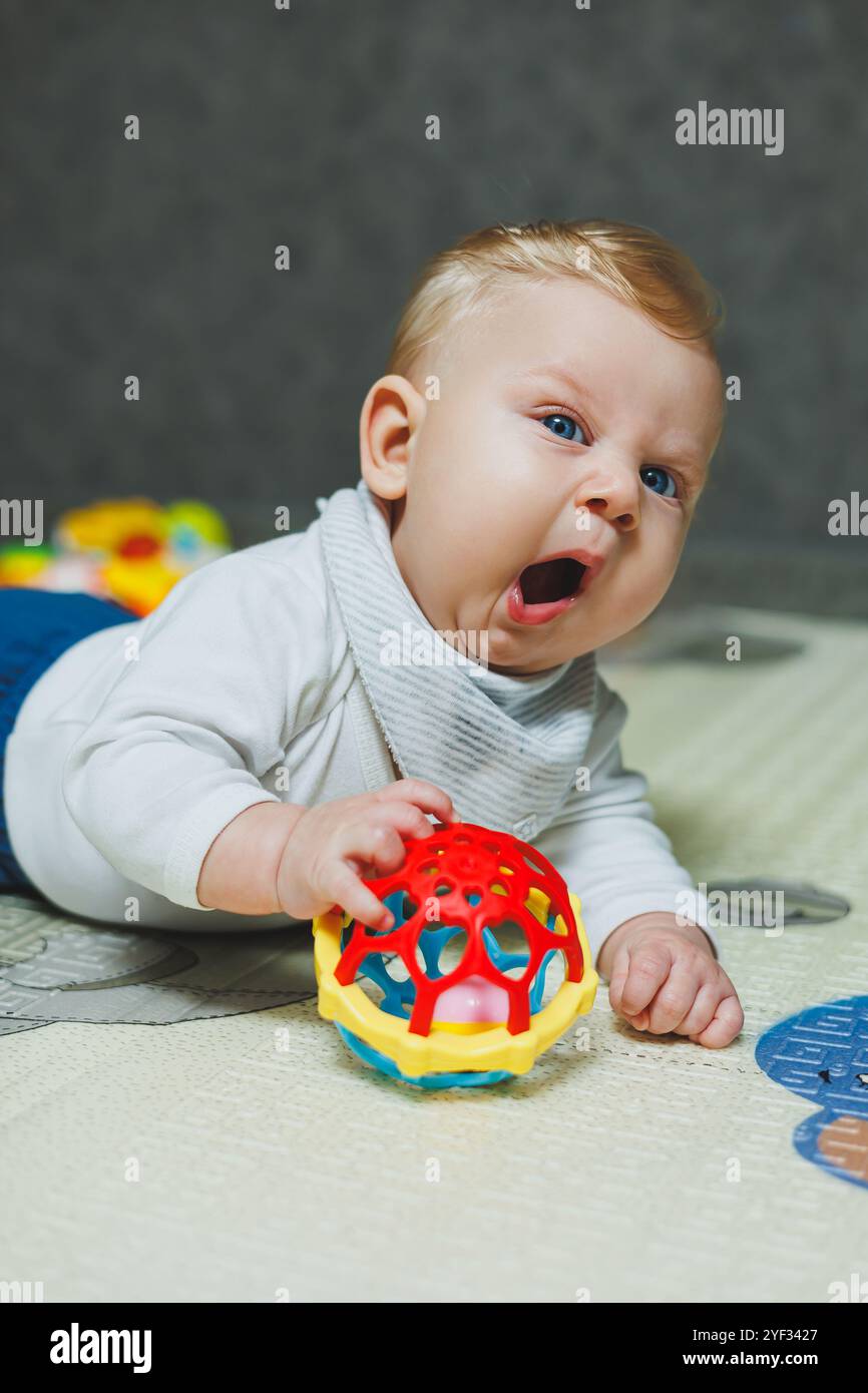 A blue-eyed baby is lying on the floor and holding his head ...