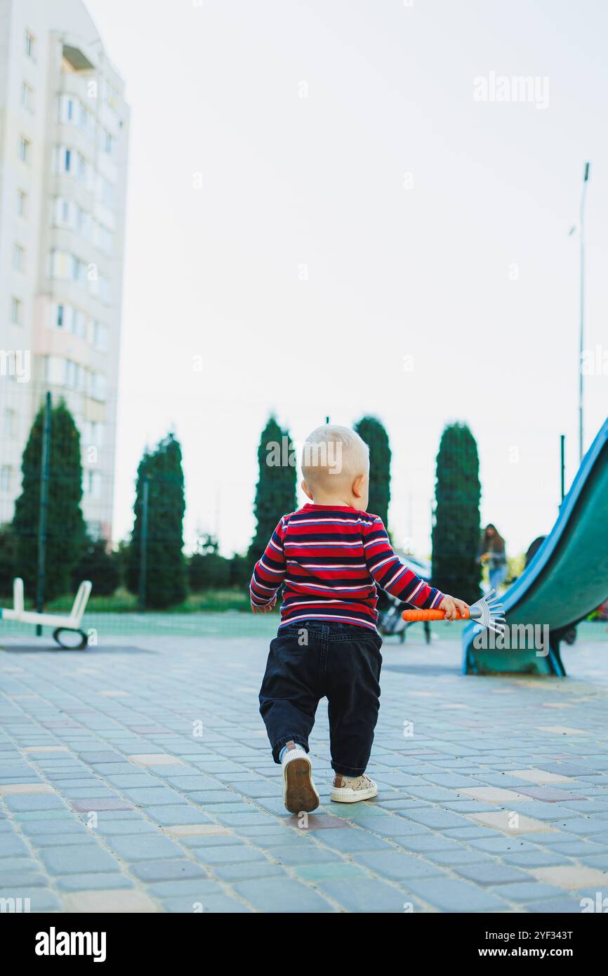 A little blond boy, 1 year old, walks on the children's playground. The ...