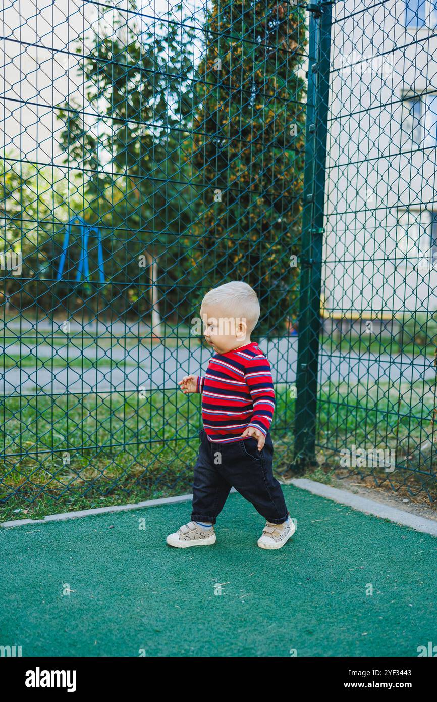 A little blond boy, 1 year old, walks on the children's playground. The ...