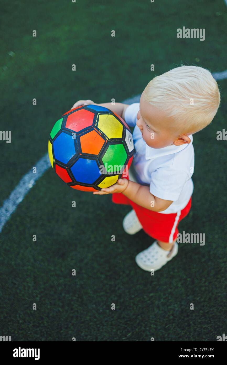 A one-year-old boy in a white T-shirt plays with a ball. TODDLER plays ...